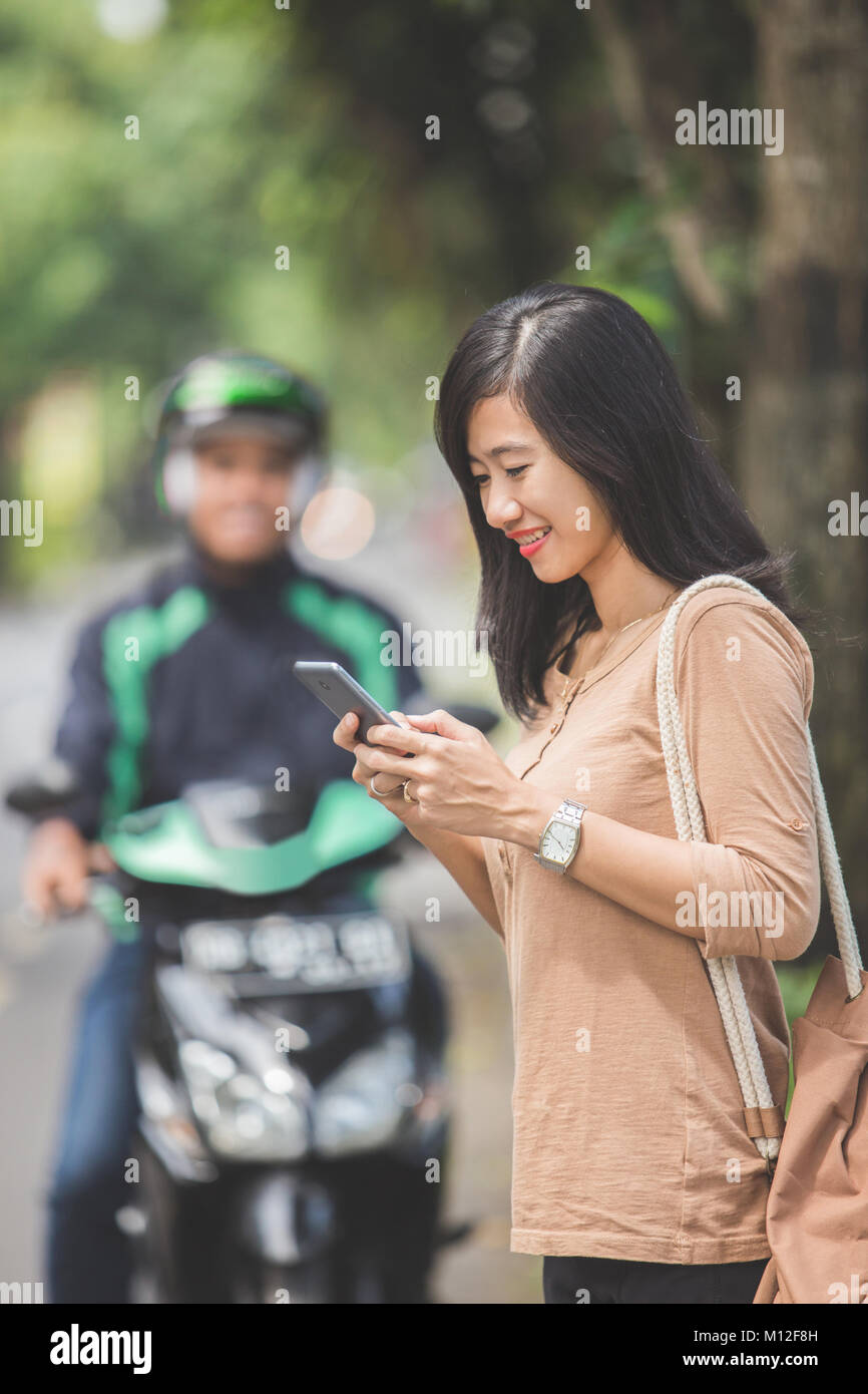 happy young woman standing on sidewalk ordering a commercial motorcycle ...