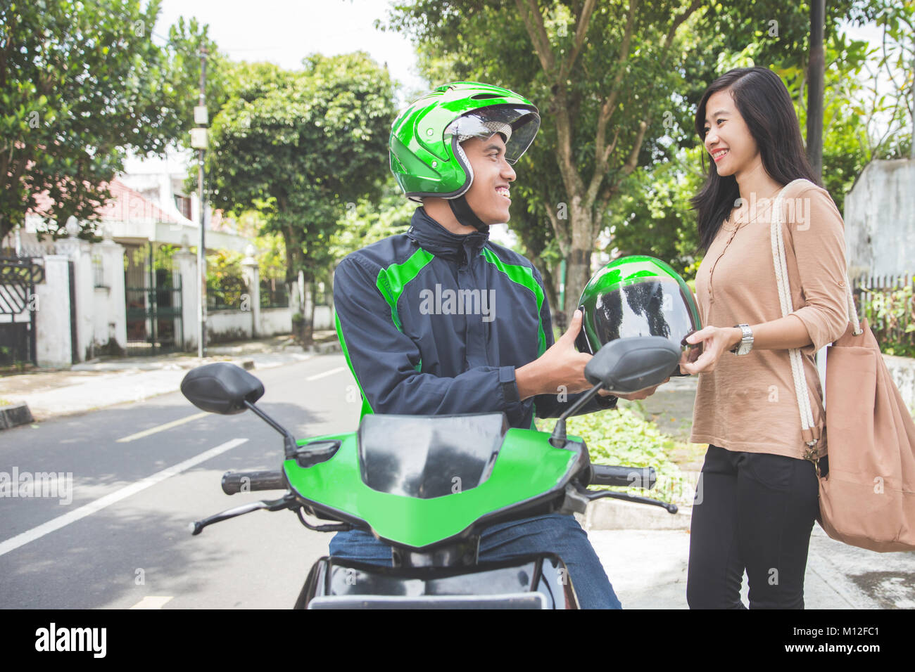 portrait of happy commercial motorcycle taxi driver giving helmet to ...