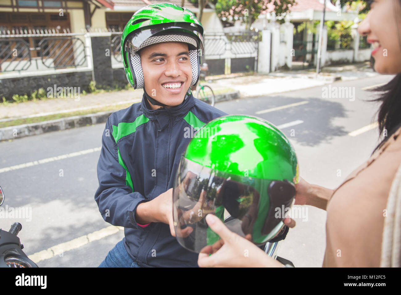 portrait of happy commercial motorcycle taxi driver giving helmet to ...