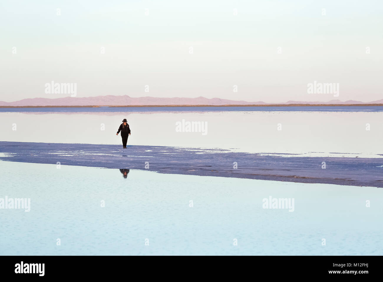Woman walking on a spit of land extending out into shallow salt water ...