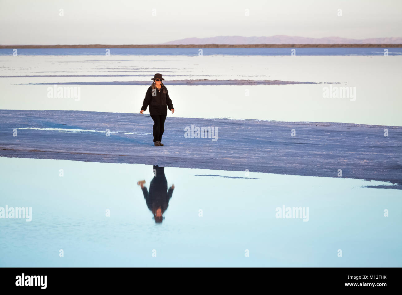 Woman walking on a spit of land extending out into shallow salt water ...