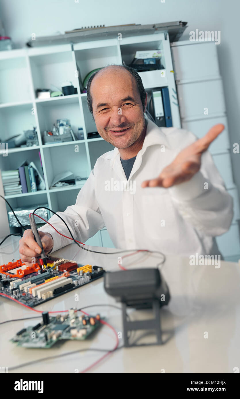 Senior male tech repairing computer motherboard smiles at the camera ...