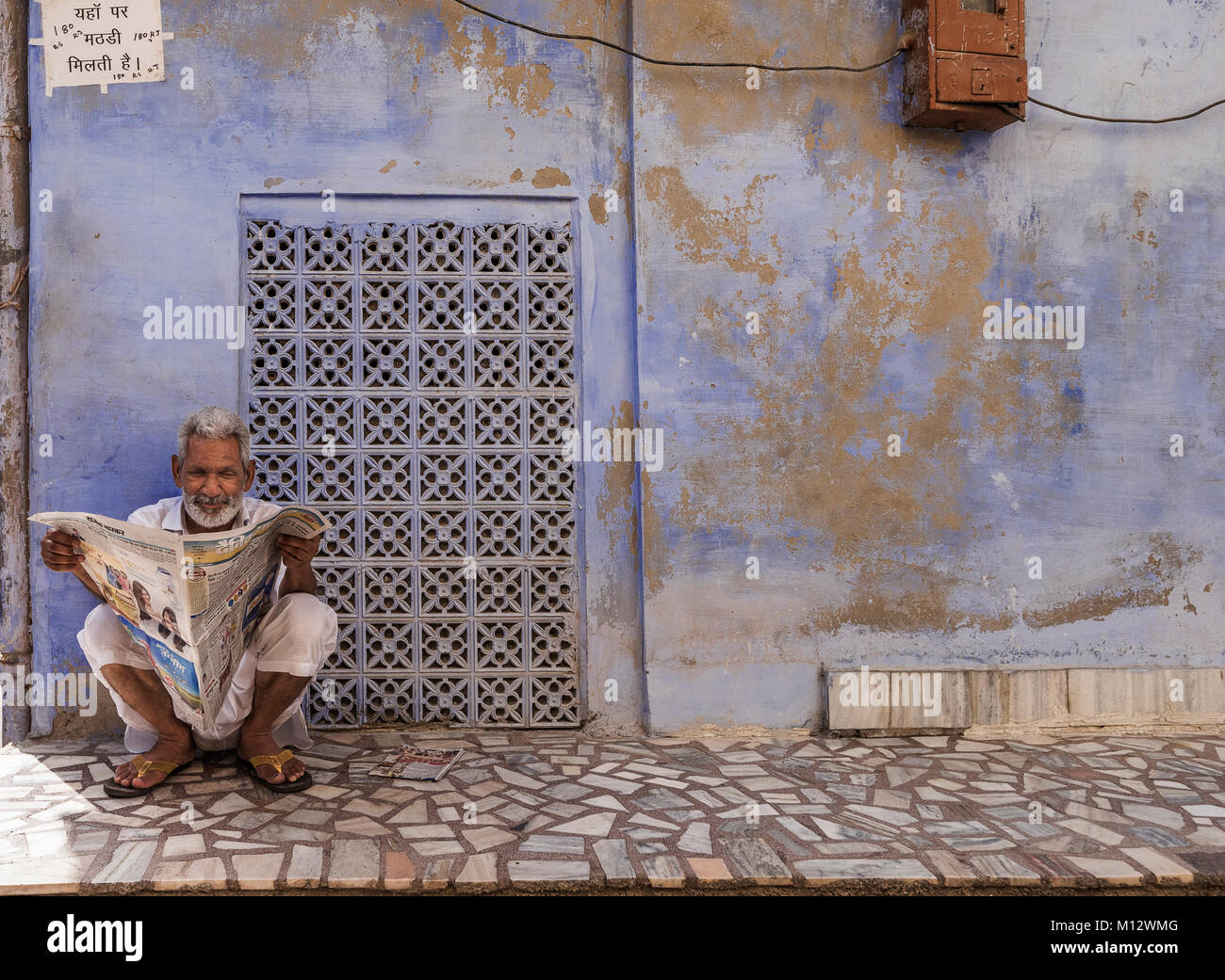 Old man reading news paper outside his blue house in Blue city of India ...