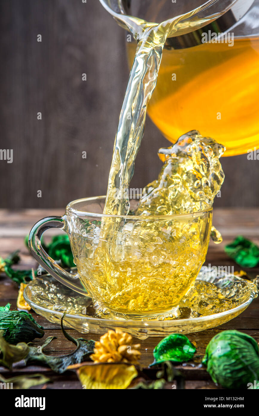 Tea poured from teapot into cup on table with dried flowers Stock Photo ...