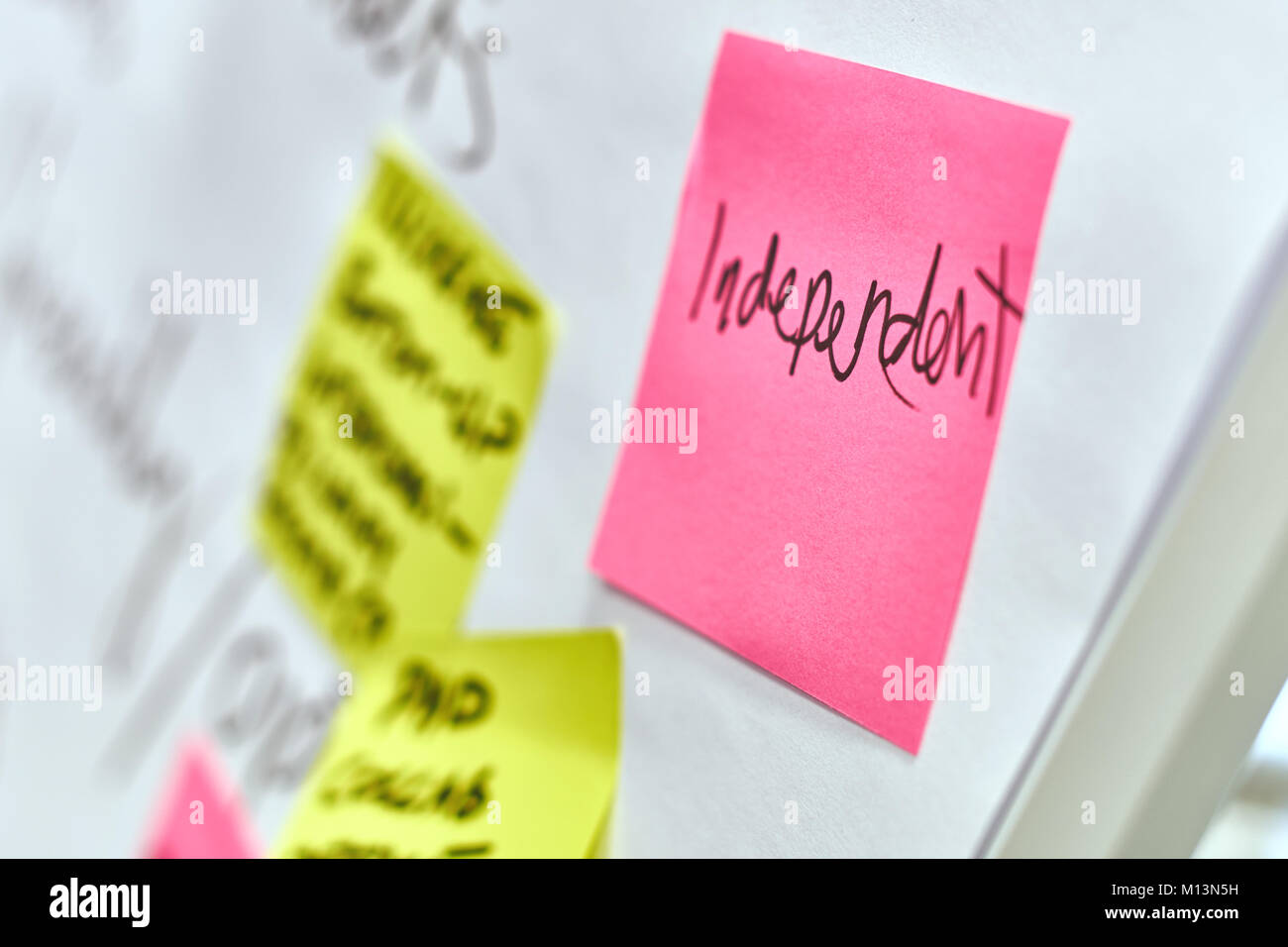 Word independent written on pink and yellow paper stickers attached to ...