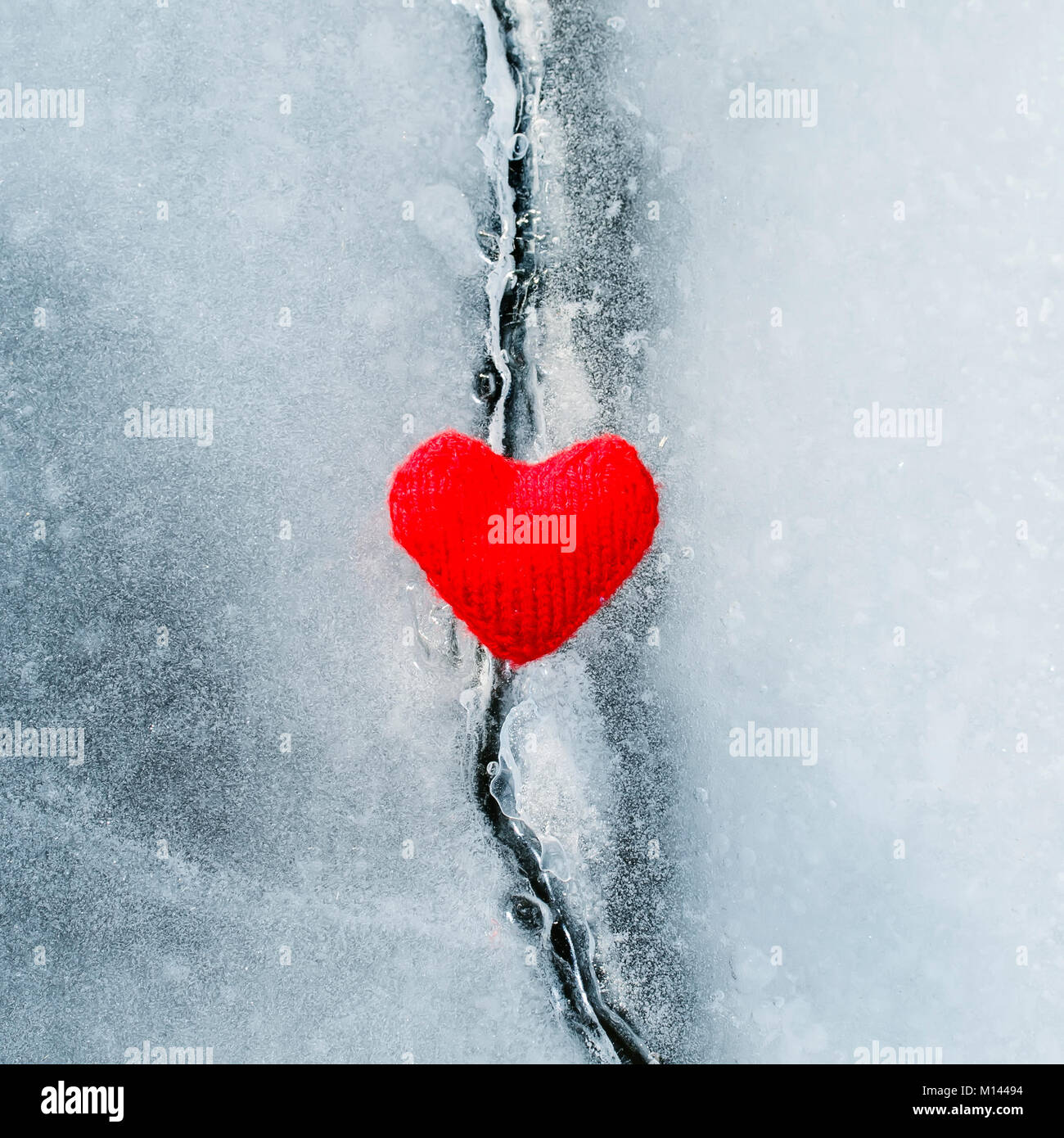 bright hot scarlet heart made of yarn lies on the clear blue cold ice ...