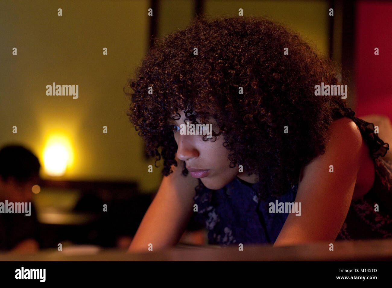 Young lady studying, with the glow of a computer screen illuminating ...