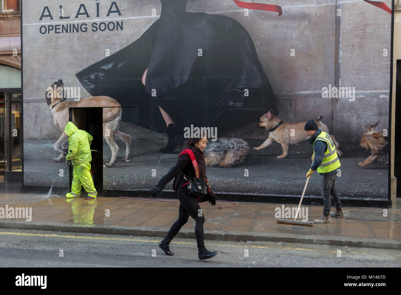 As workmen hose down the muddy pavement, a passer-by carefully walks ...