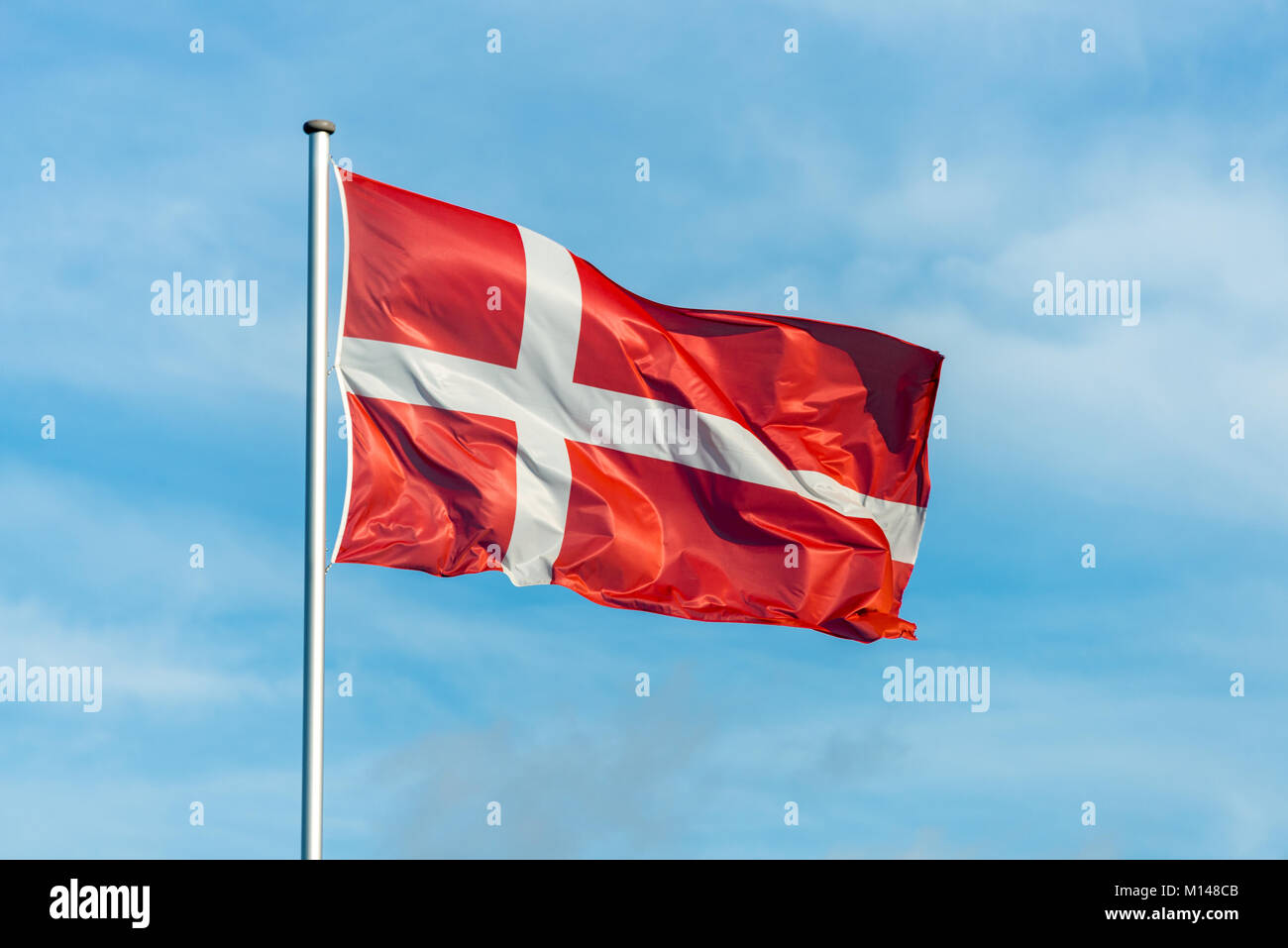 Closeup of single danish flag waving in the wind in front of blue sky ...