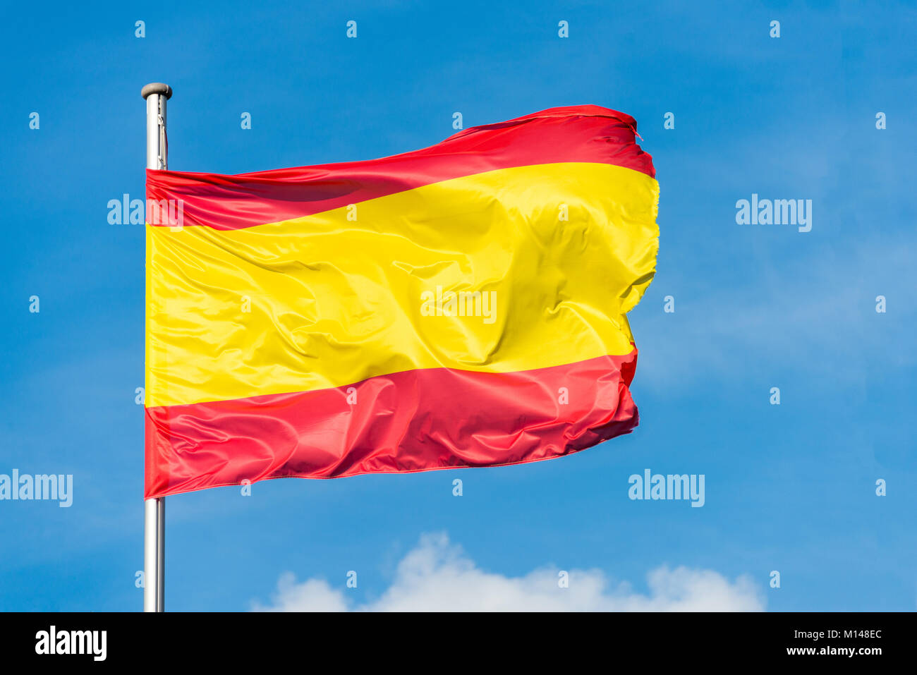 Closeup of single spanish flag waving in the wind in front of blue sky ...