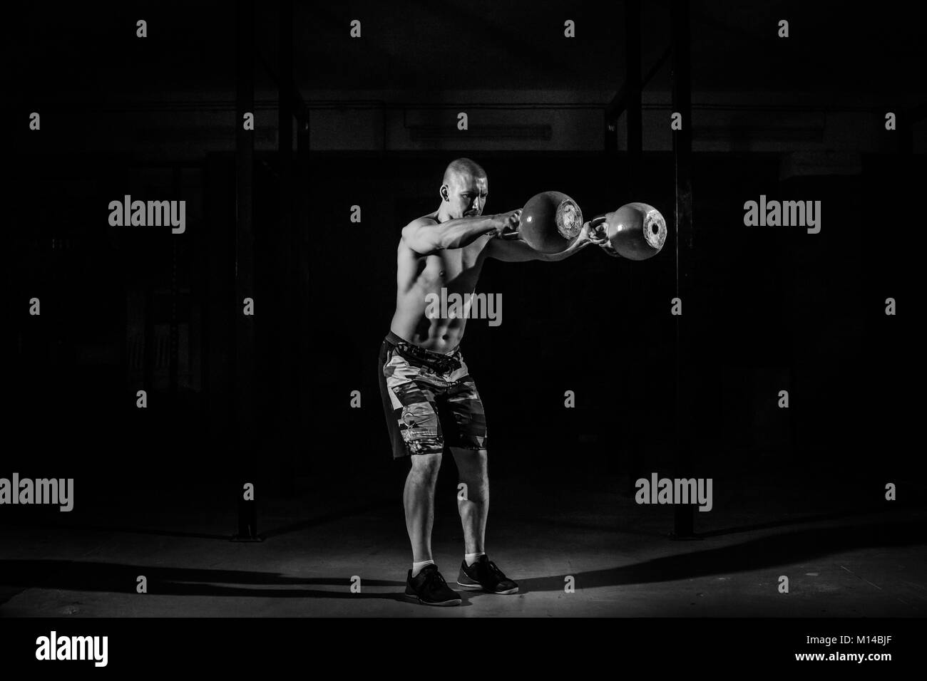 A strong man picks up kettlebell in gym. Kettlebell lifting. Black and ...