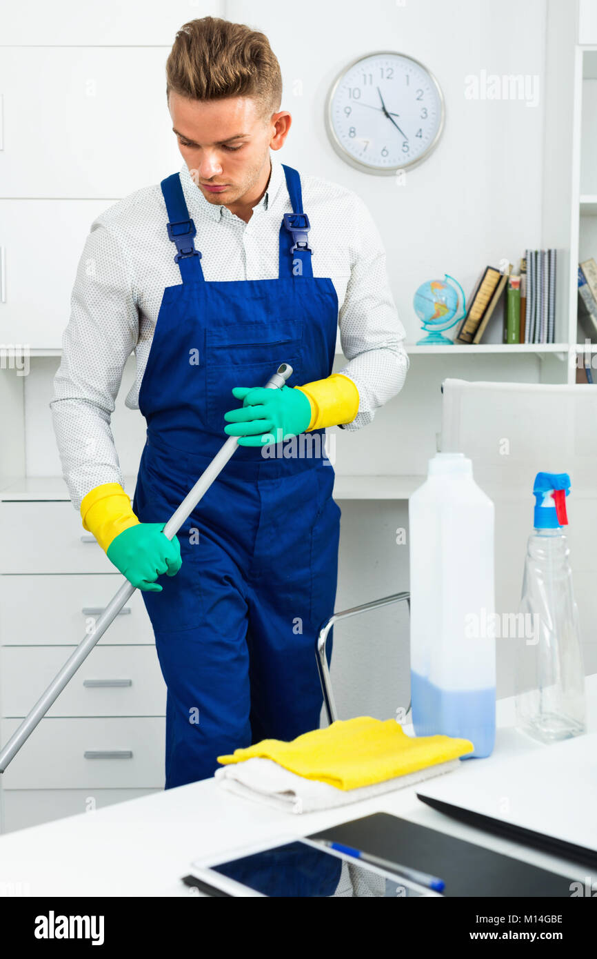 Diligent male professional janitor dusting in modern office interior ...