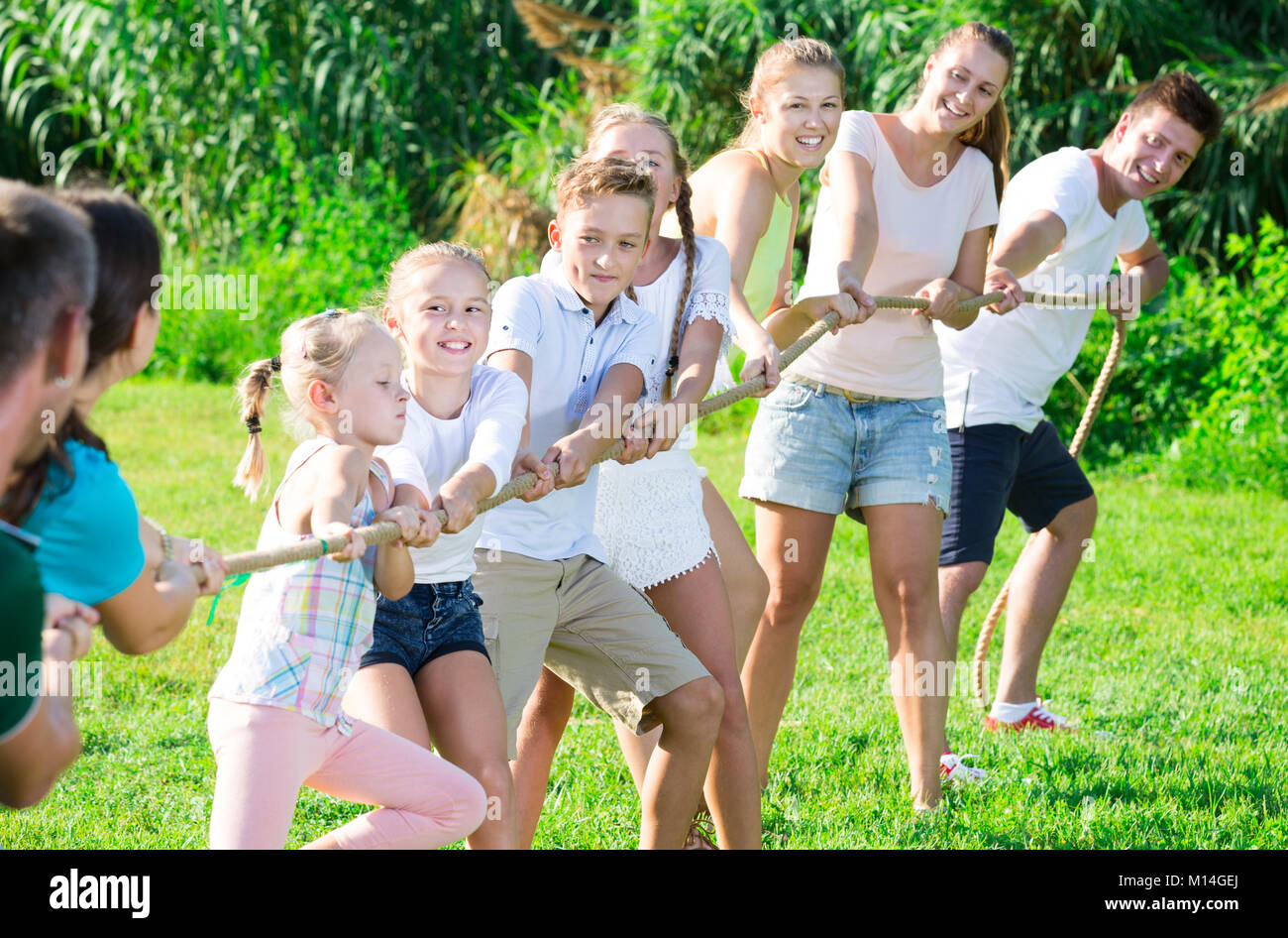 Kids with adult moms and dads playing tug of war during joint outdoors ...