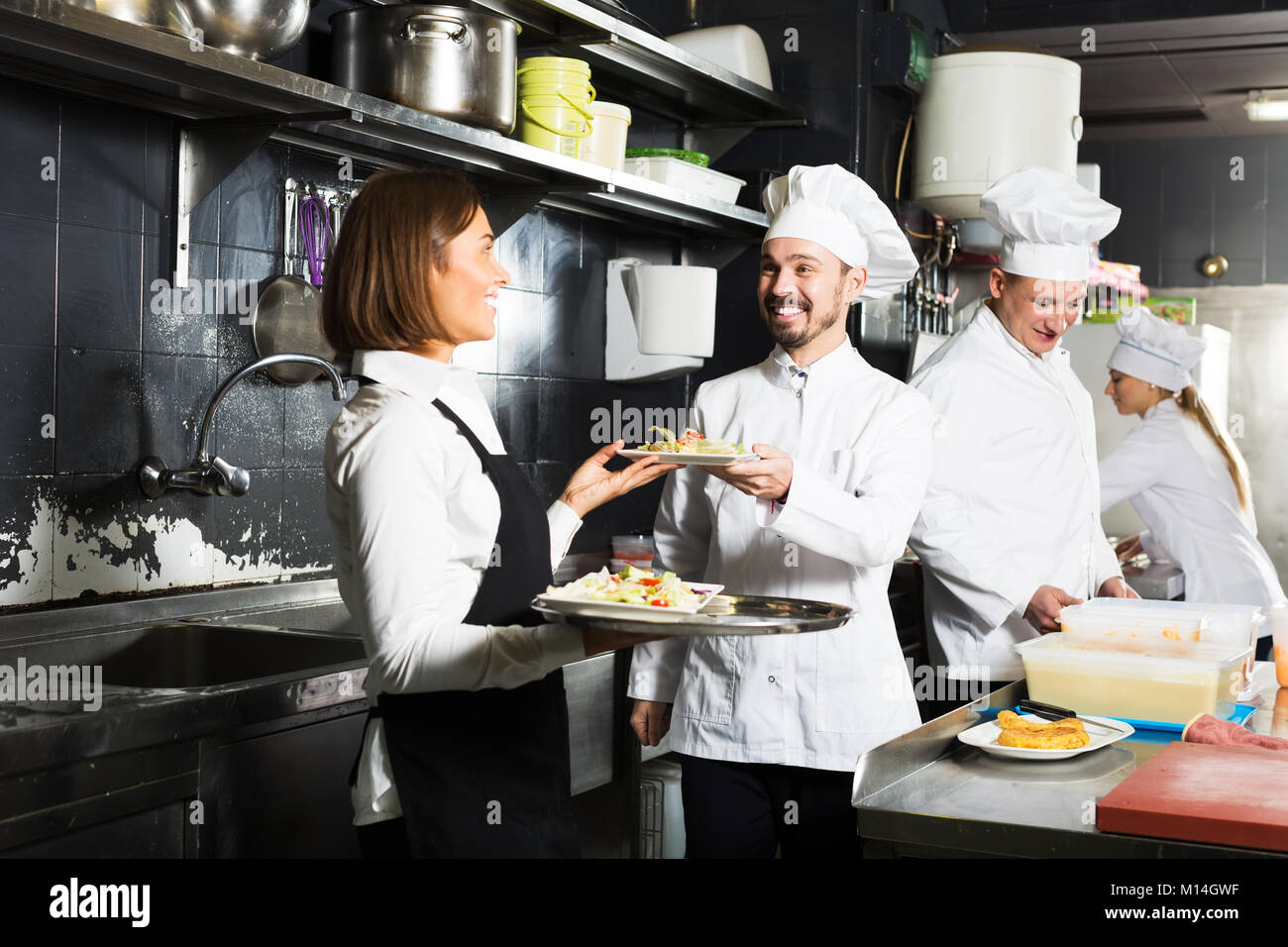 Young positive female waiter taking order of meal from restaurant’s ...