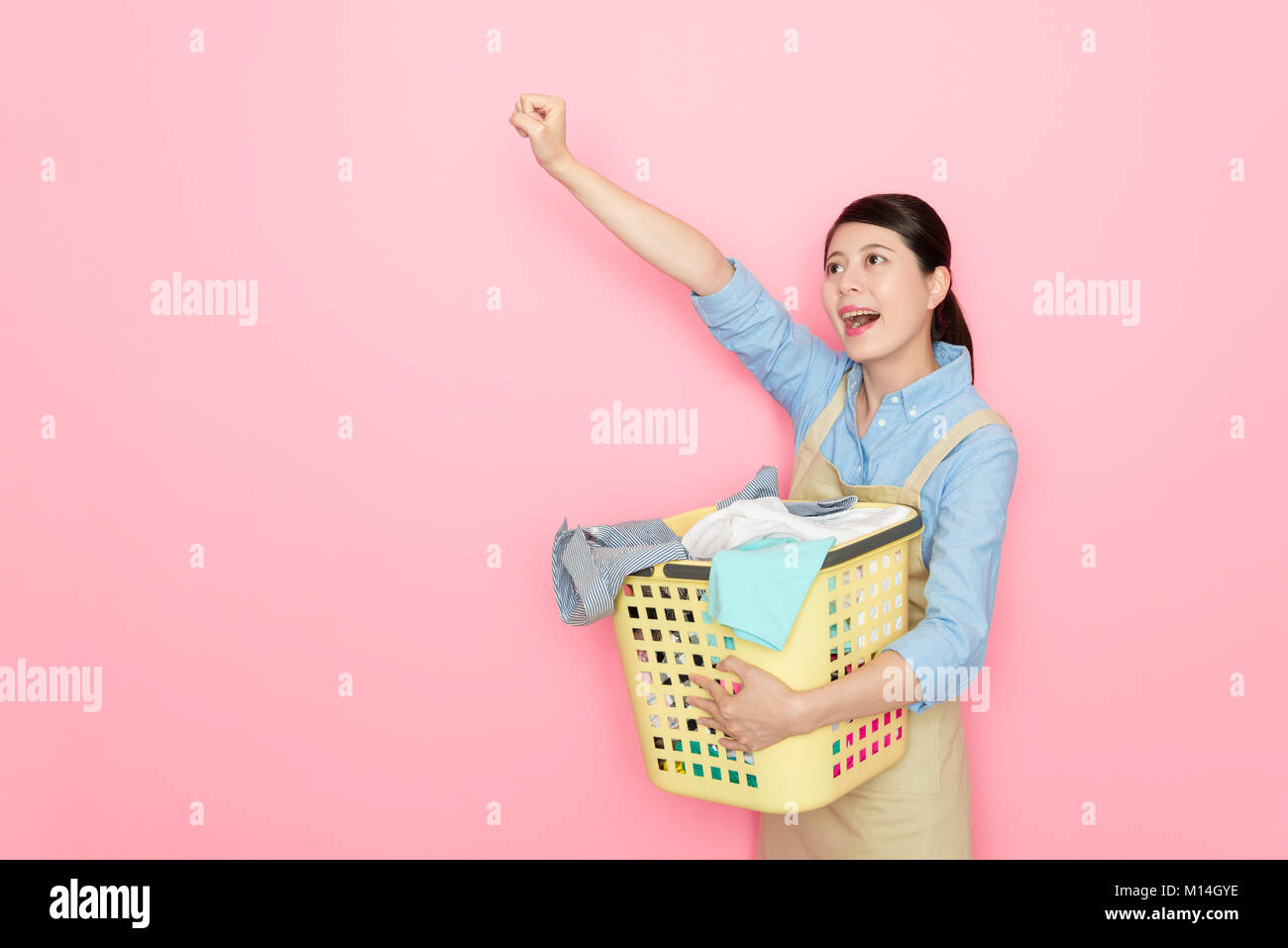 cheerful pretty female housekeeper holding clothing basket and raised ...