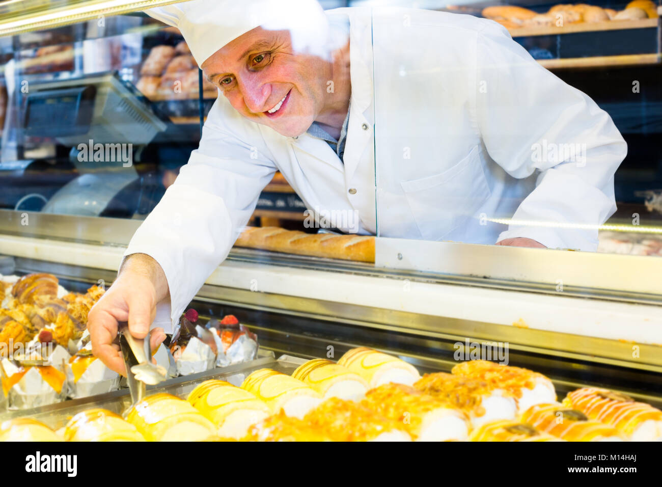Mature male distributor offering fresh pastry in sweet-shop Stock Photo ...
