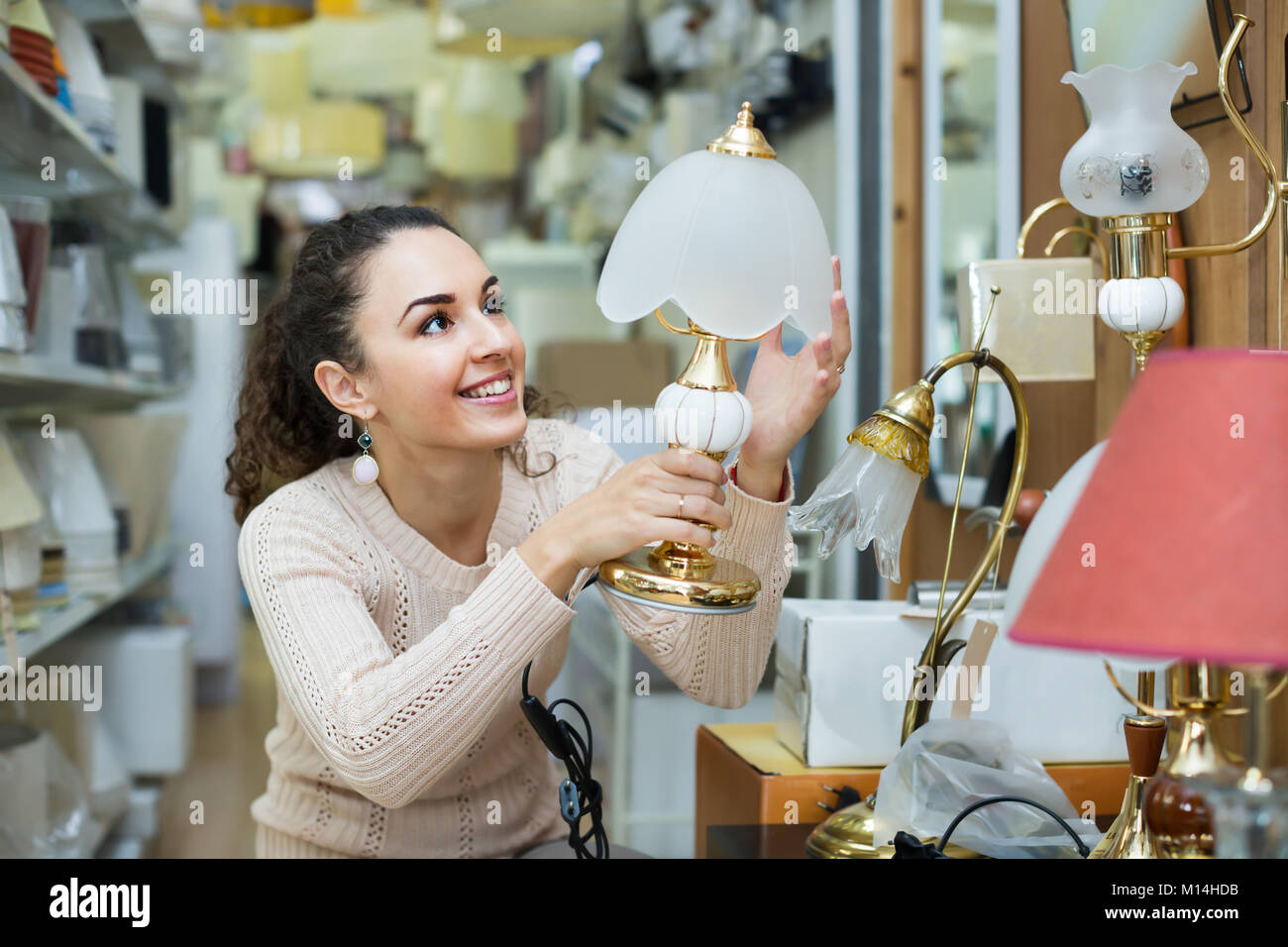 Modern woman selecting lighting units for interior in household store ...