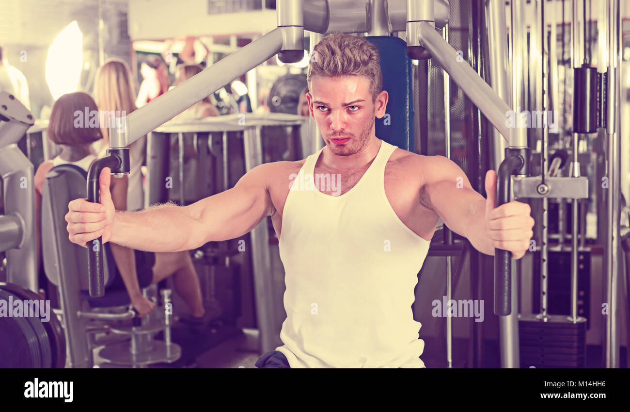 young european well trained man using pec deck gym machinery indoors ...