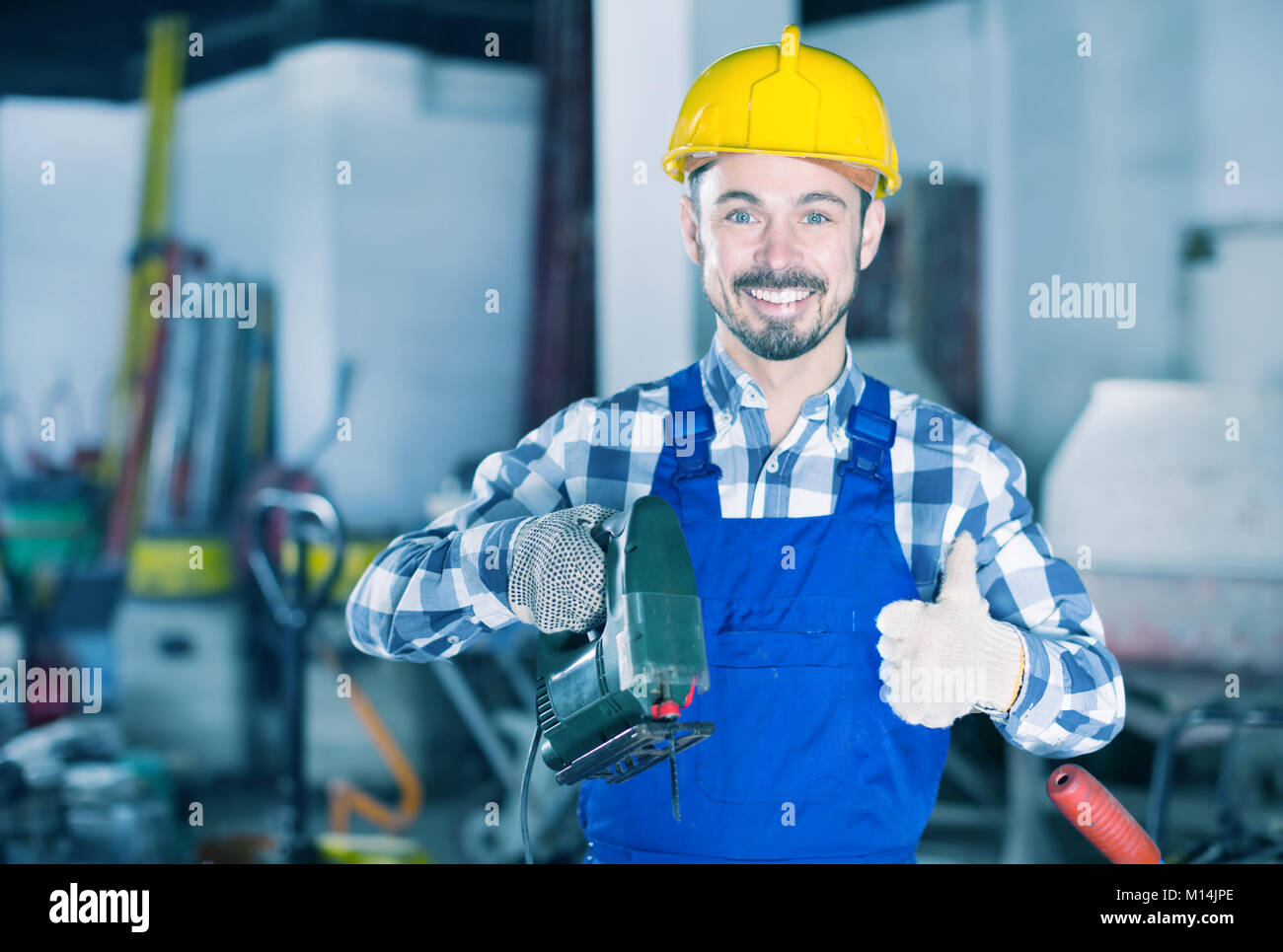 Smiling working man practicing his skills with power jigsaw in the ...