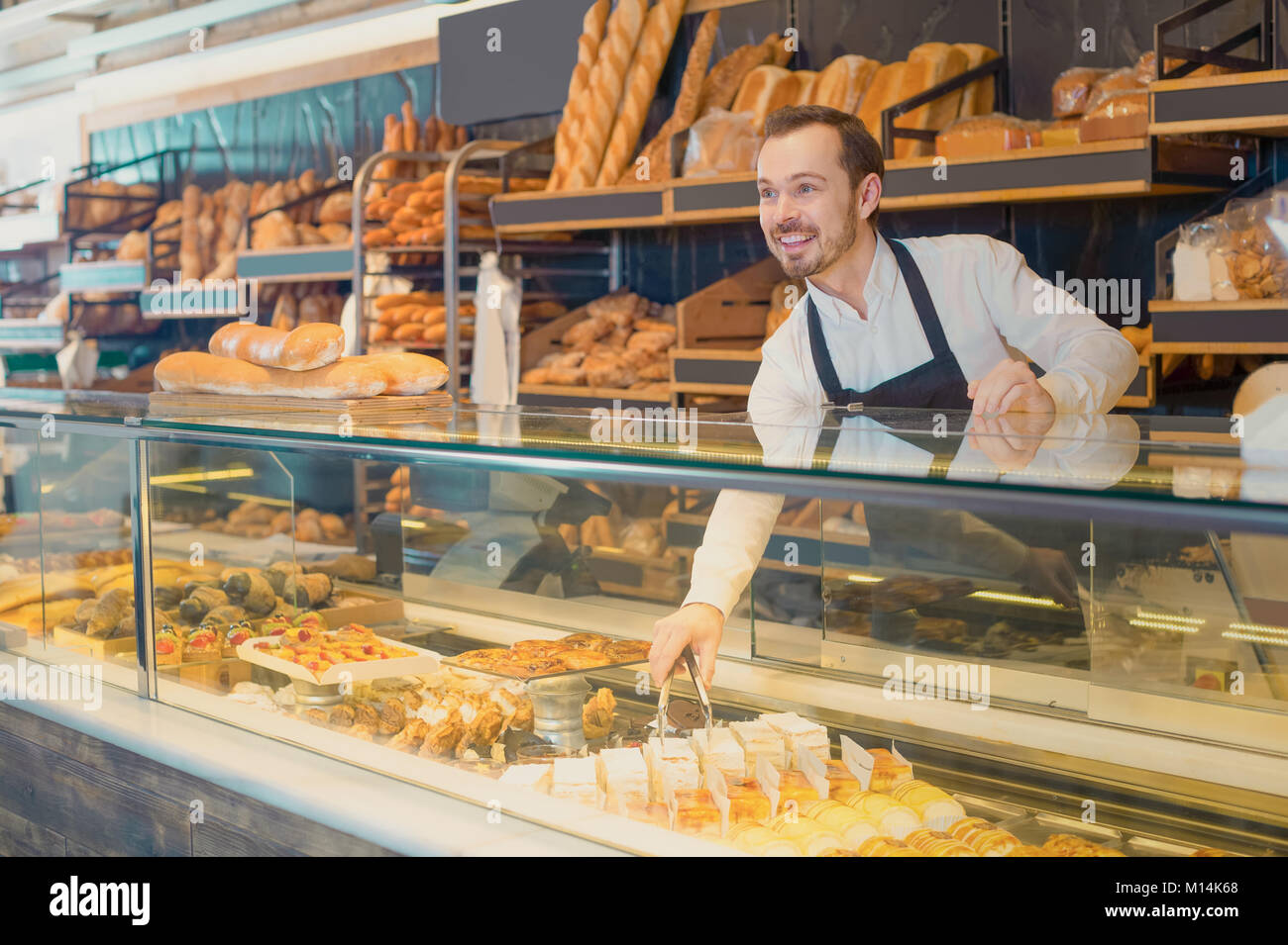 happy english male shop assistant demonstrating fresh delicious pastry ...