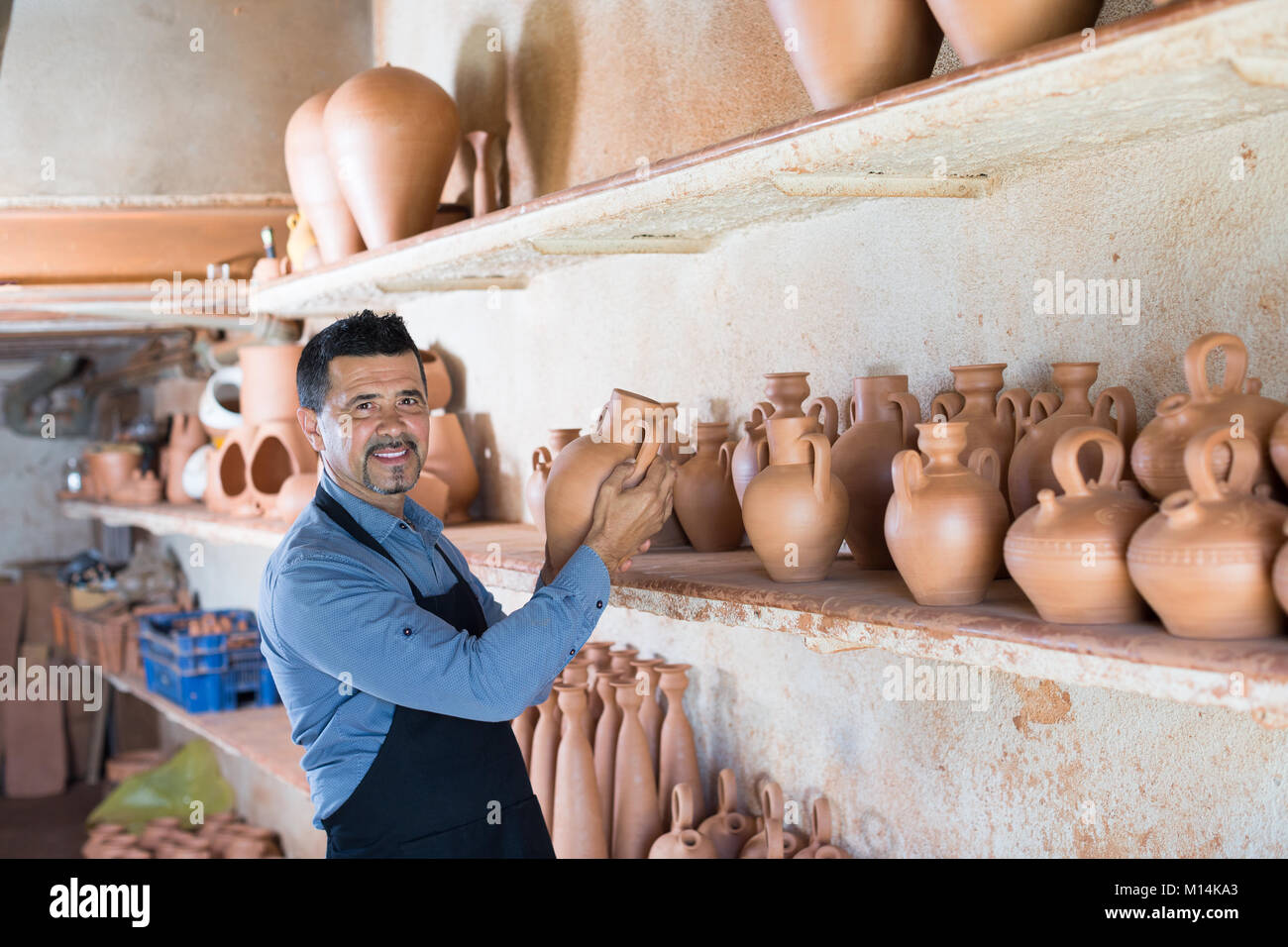 Smiling male sculptor having ceramics in hands and standing in pottery ...