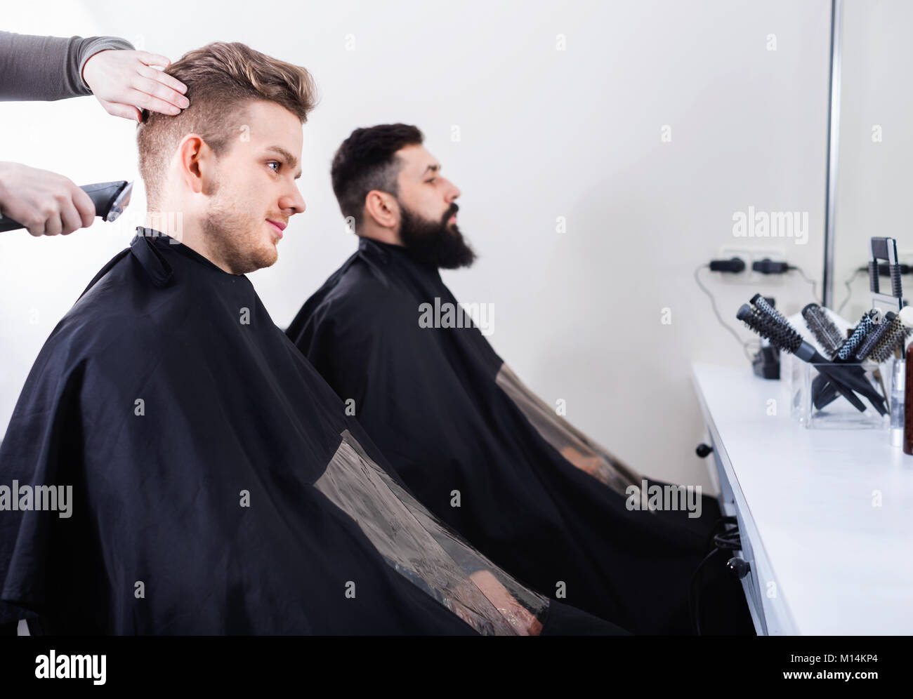 Young positive smiling efficient clients having their hair cut by ...