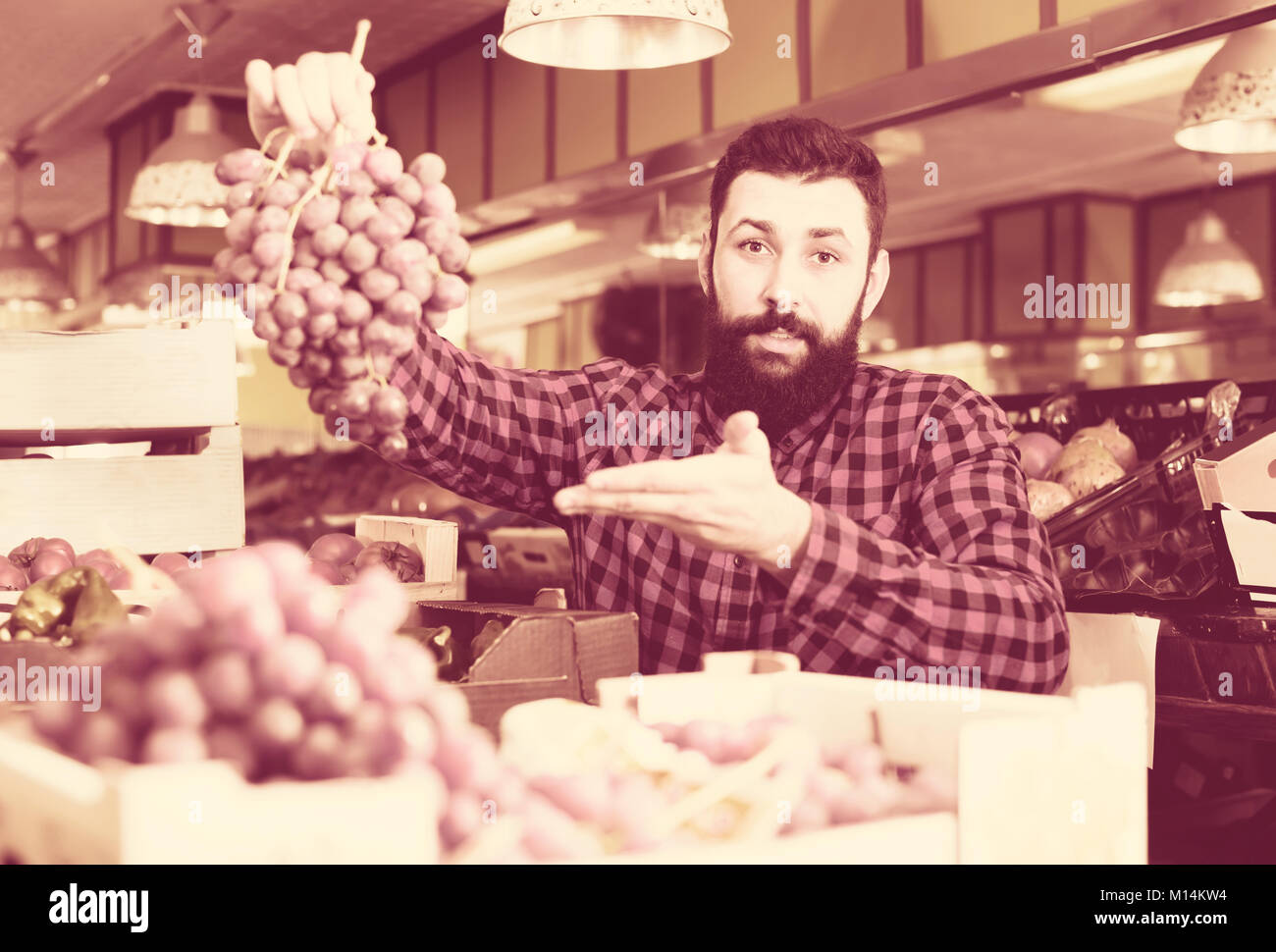 Adult male seller offering grapes in grocery shop Stock Photo - Alamy