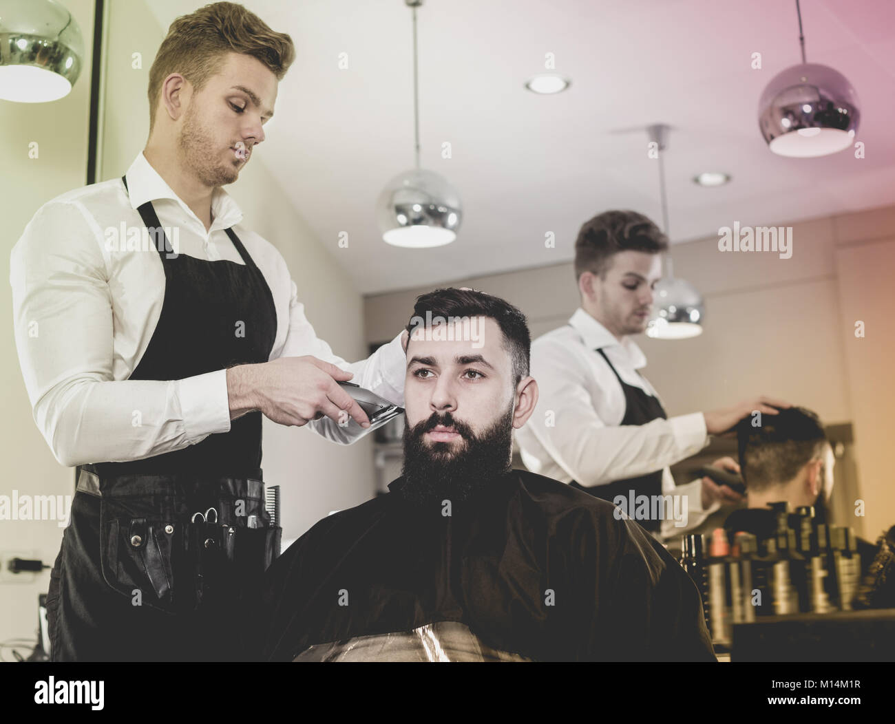 Handsome guy stylist creating new shape for beard of client at ...