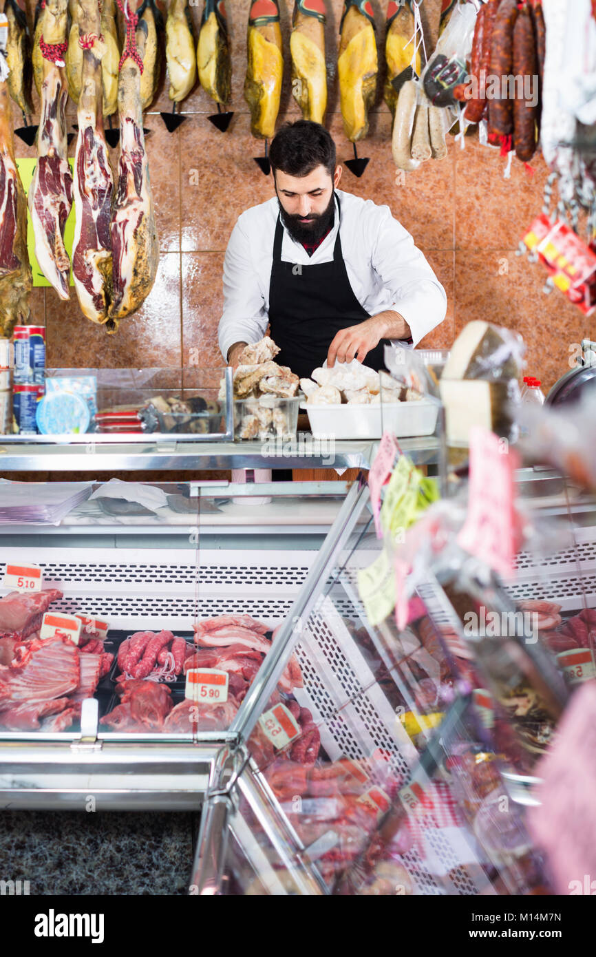 Positive man seller grouping meat to sell in butcher’s shop Stock Photo ...