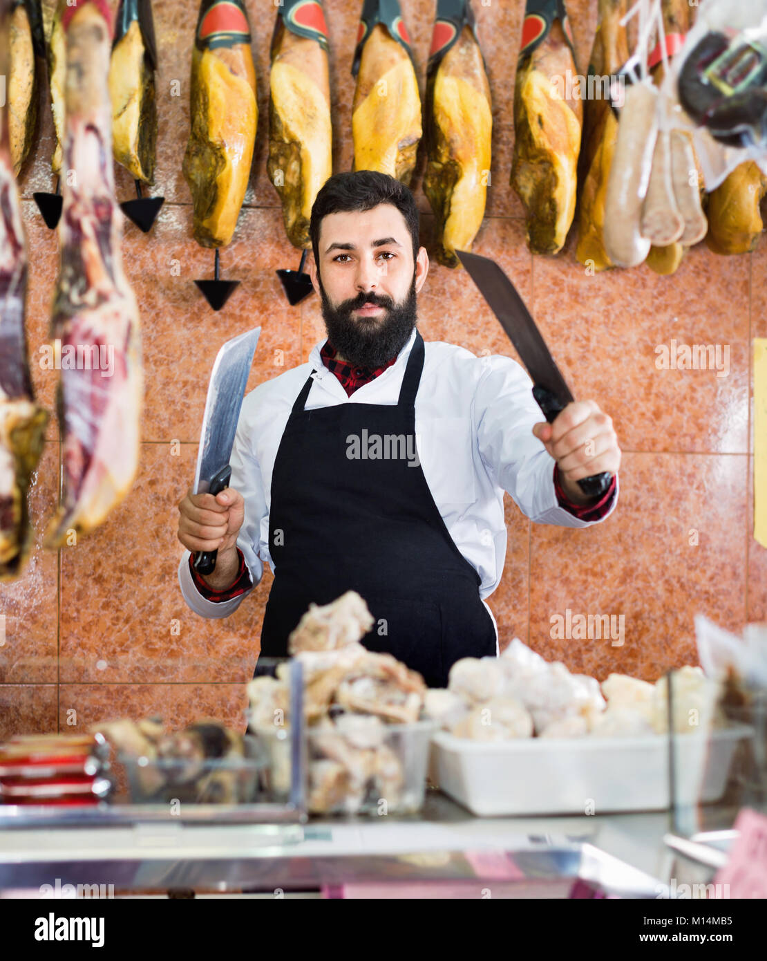 Smiling positive man seller preparing meat to sell in butcher’s shop ...