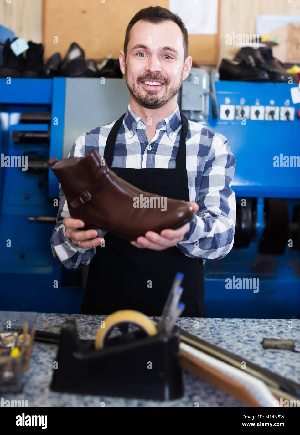 Adult male worker showing fixed shoes in shoe repair workshop Stock ...