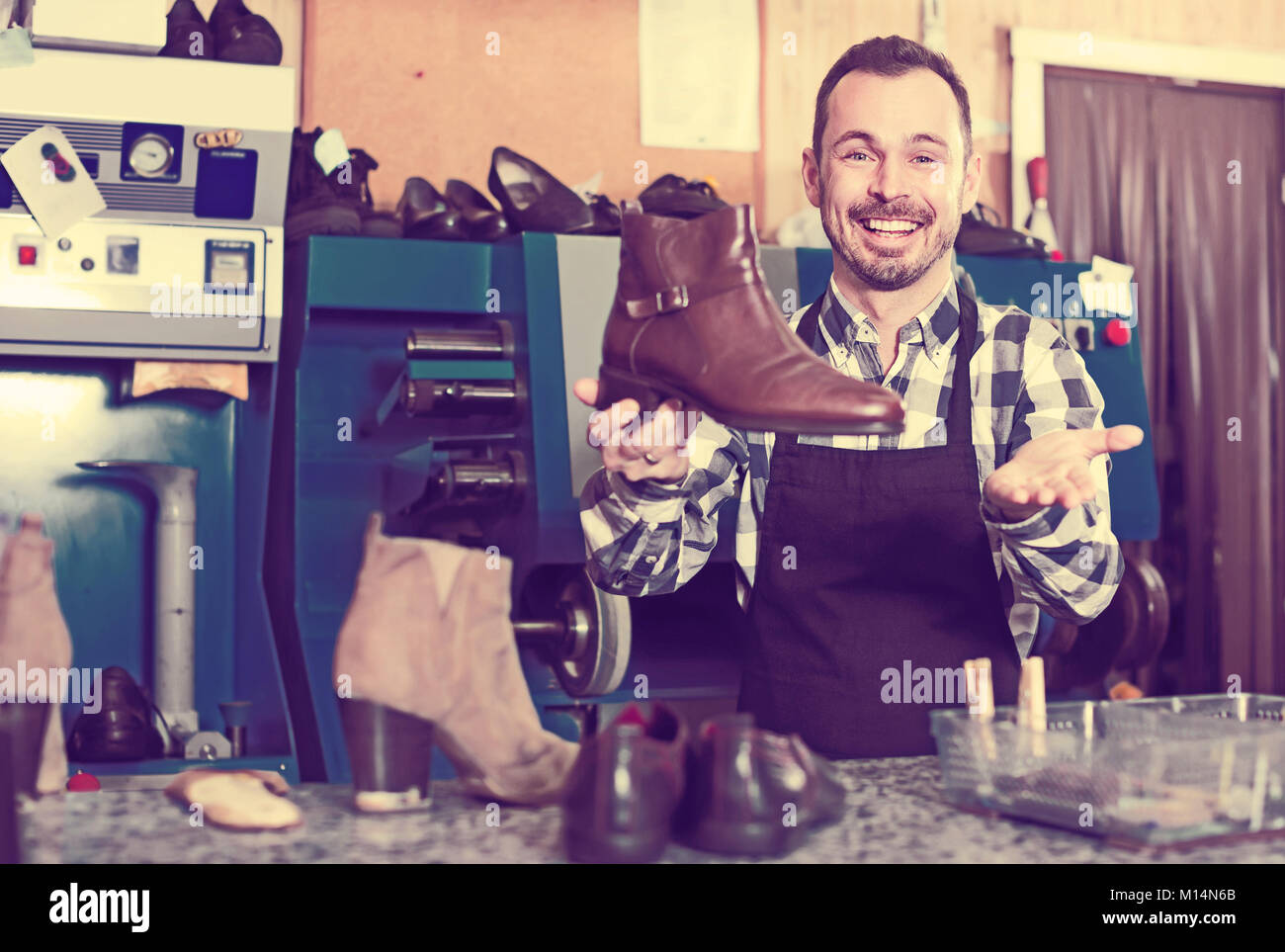 Glad male worker showing fixed shoes in shoe repair workshop Stock ...
