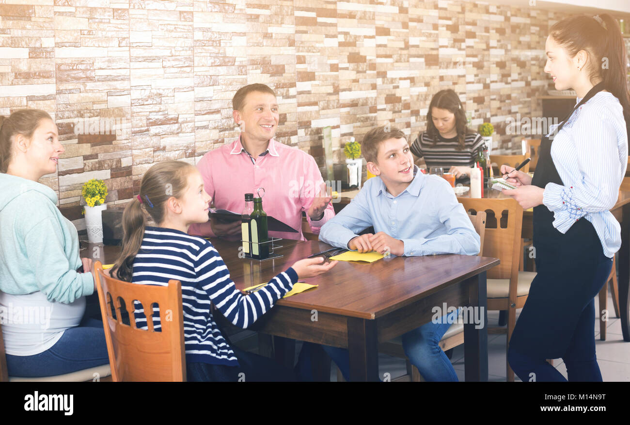 Hospitable waitress helping visitors with menu taking order in cafe ...