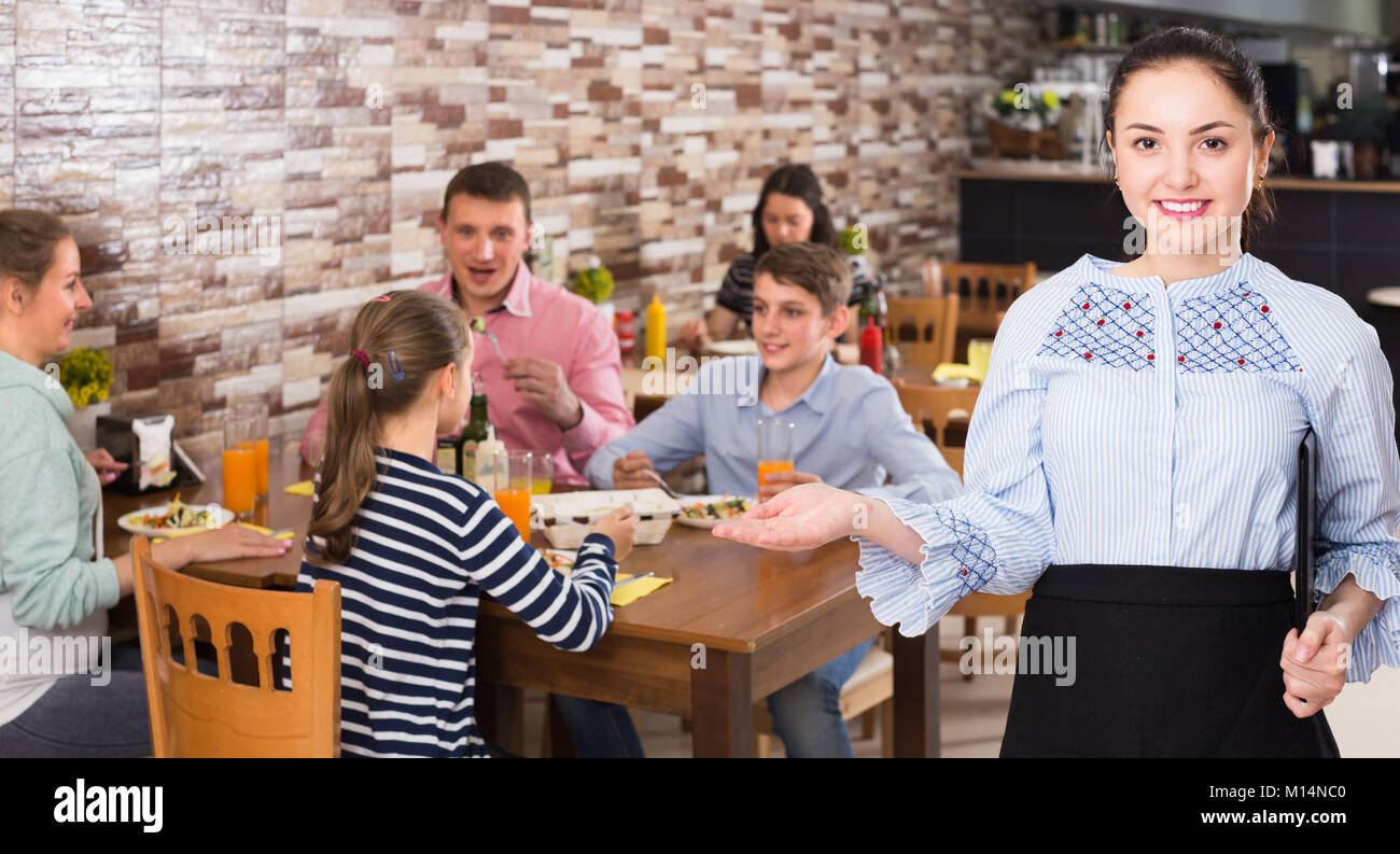 Professional waitress holding tray with dishes meeting visitors in cafe ...