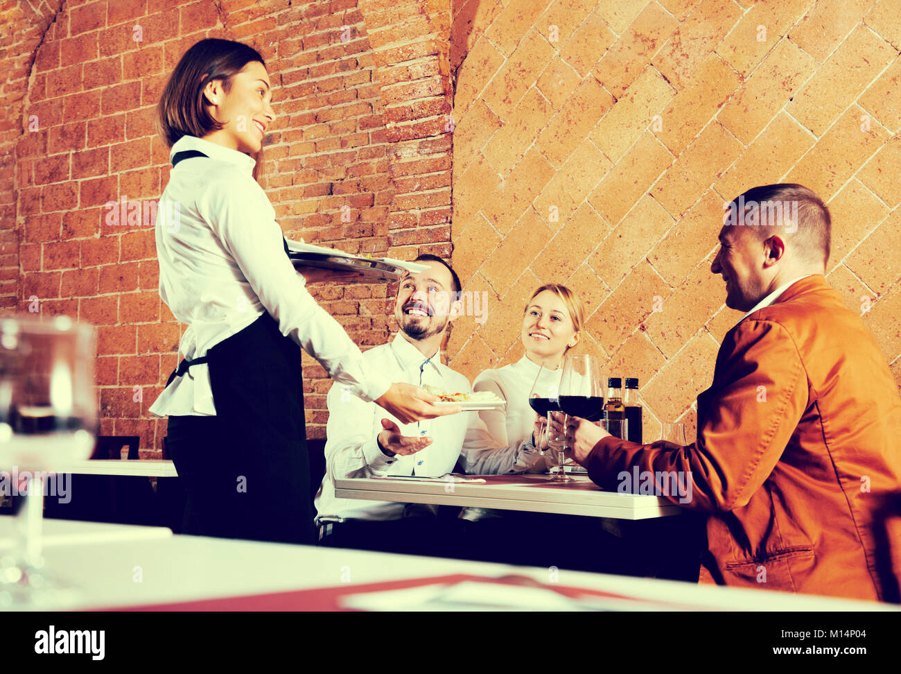 Young female waiter carrying order for visitors in country restaurant ...