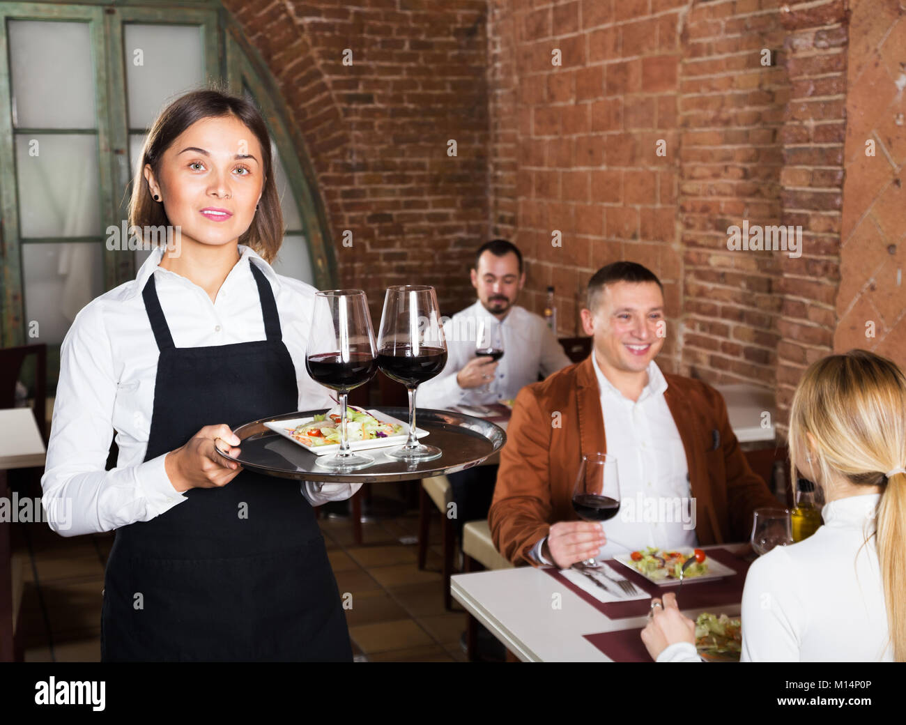 Smiling female waiter welcoming visitors to country restaurant Stock ...