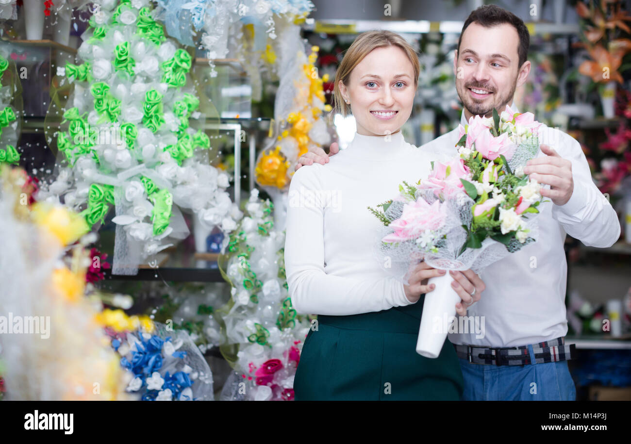 Glad loving couple deciding on colorful flower decoration in store ...