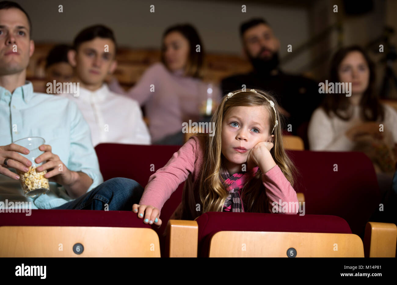Sad little girl watching boring movie in cinema house Stock Photo - Alamy