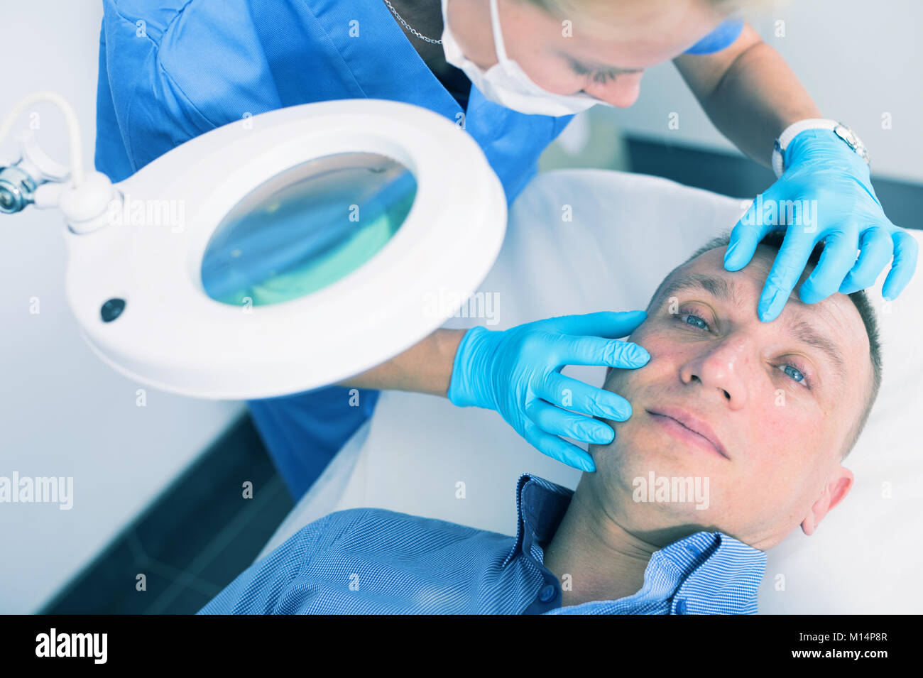 Woman specialist is cleaning skin of patient with using magnification ...