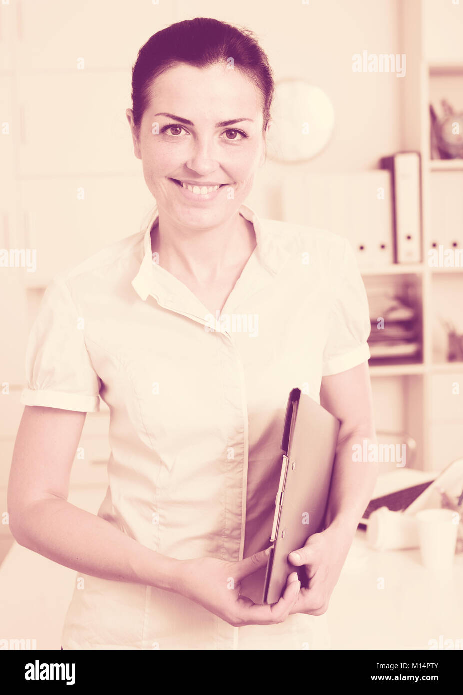 Cheerful office worker at workplace standing with folder indoors Stock ...