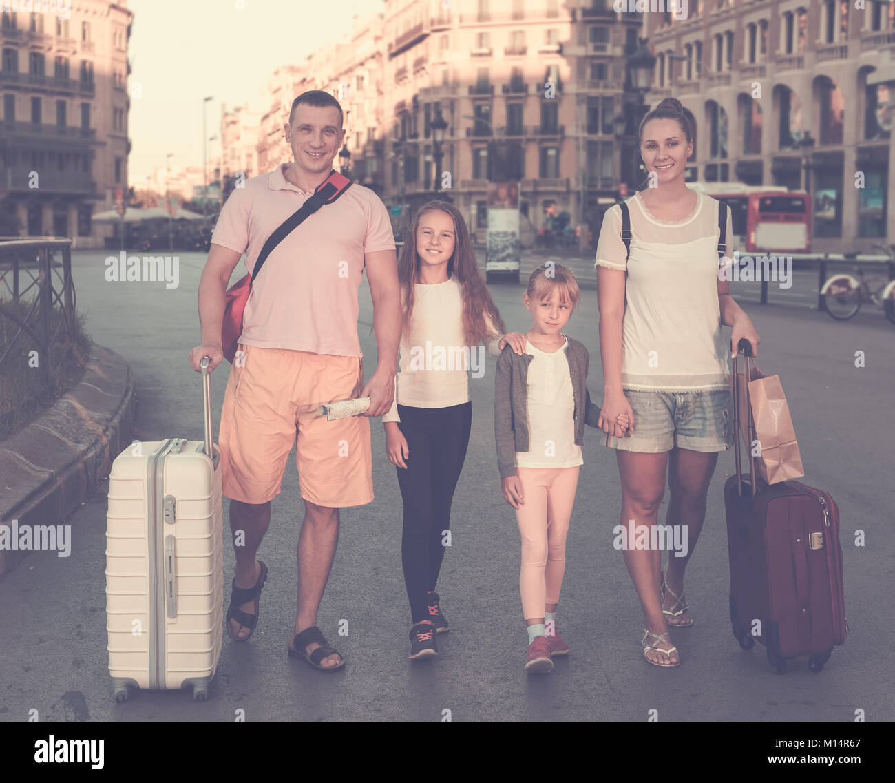 Happy family of four travelling together on city, walking with baggage ...