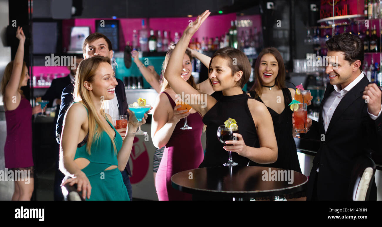 Cheerful positive colleagues dancing on corporate party with cocktails ...