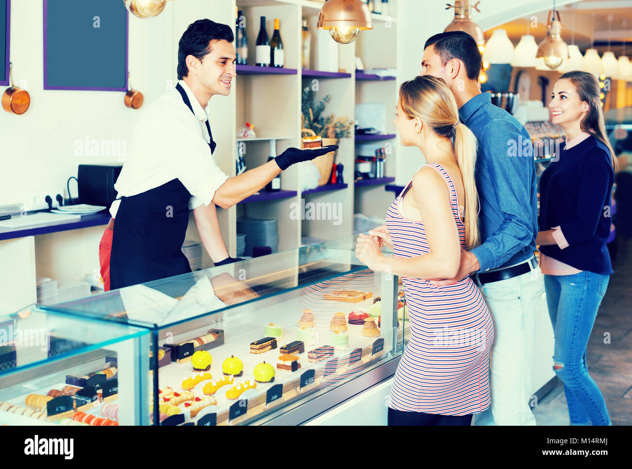 Couple with female friend are choosing cakes from showcase in pastry ...