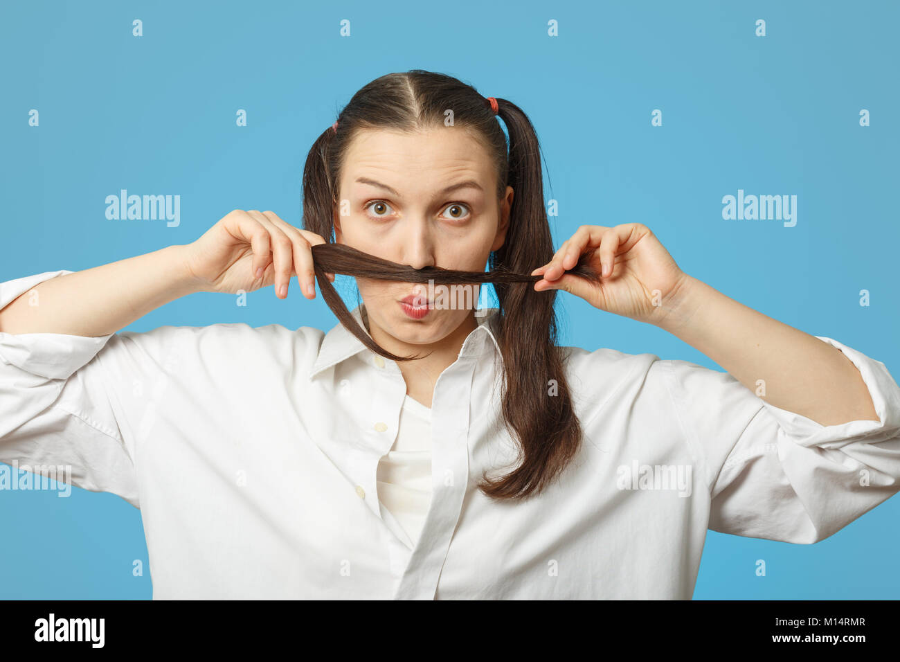 pretty young woman on blue background making mustache with her hair ...