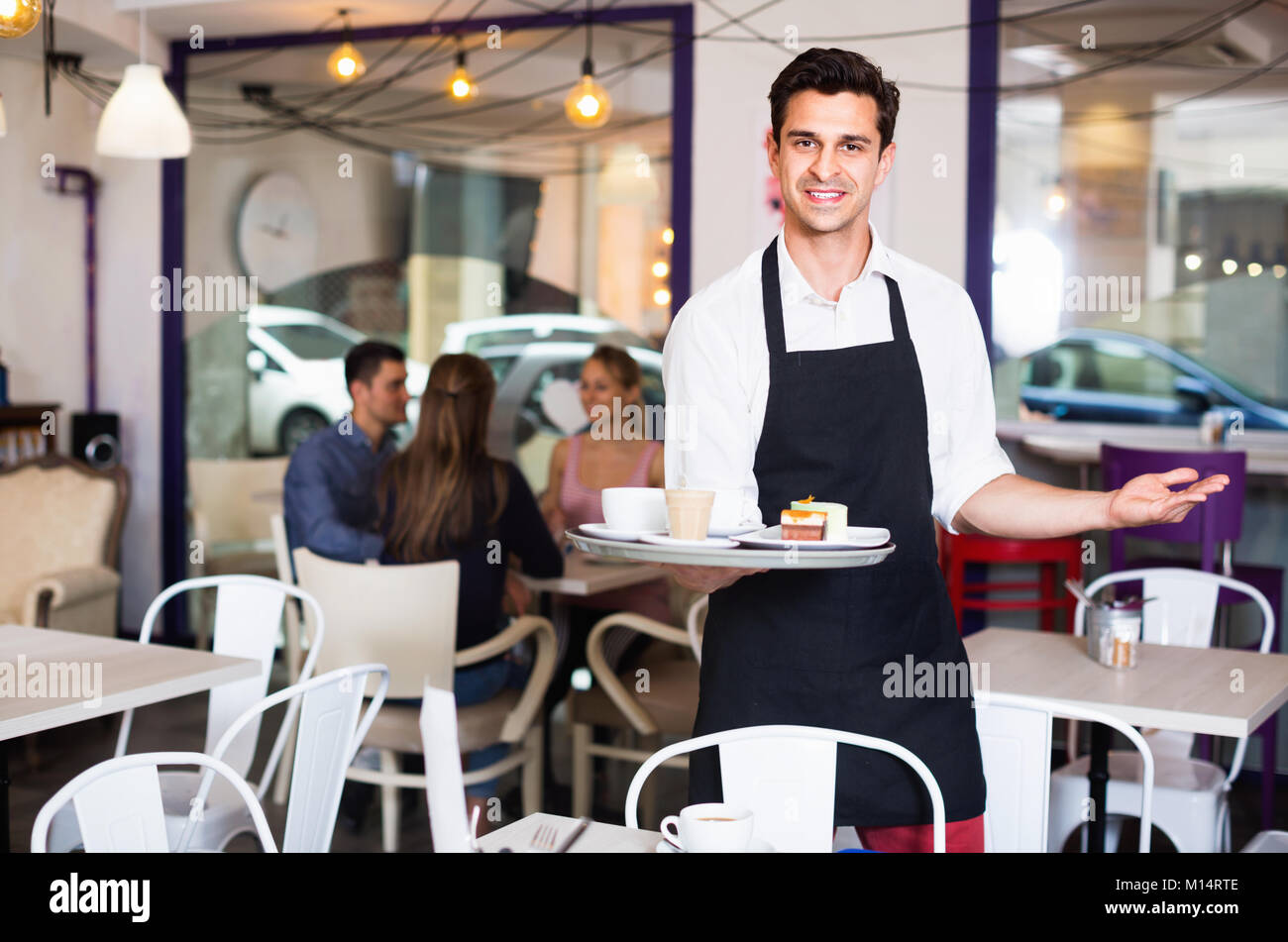 Cheerful positive waiter holding served tray meeting visitors at pastry ...