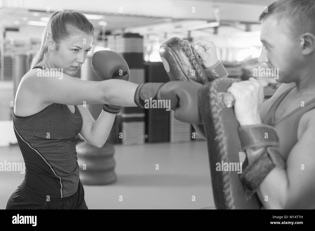 Young female is training punch with male trainer in fitness center ...