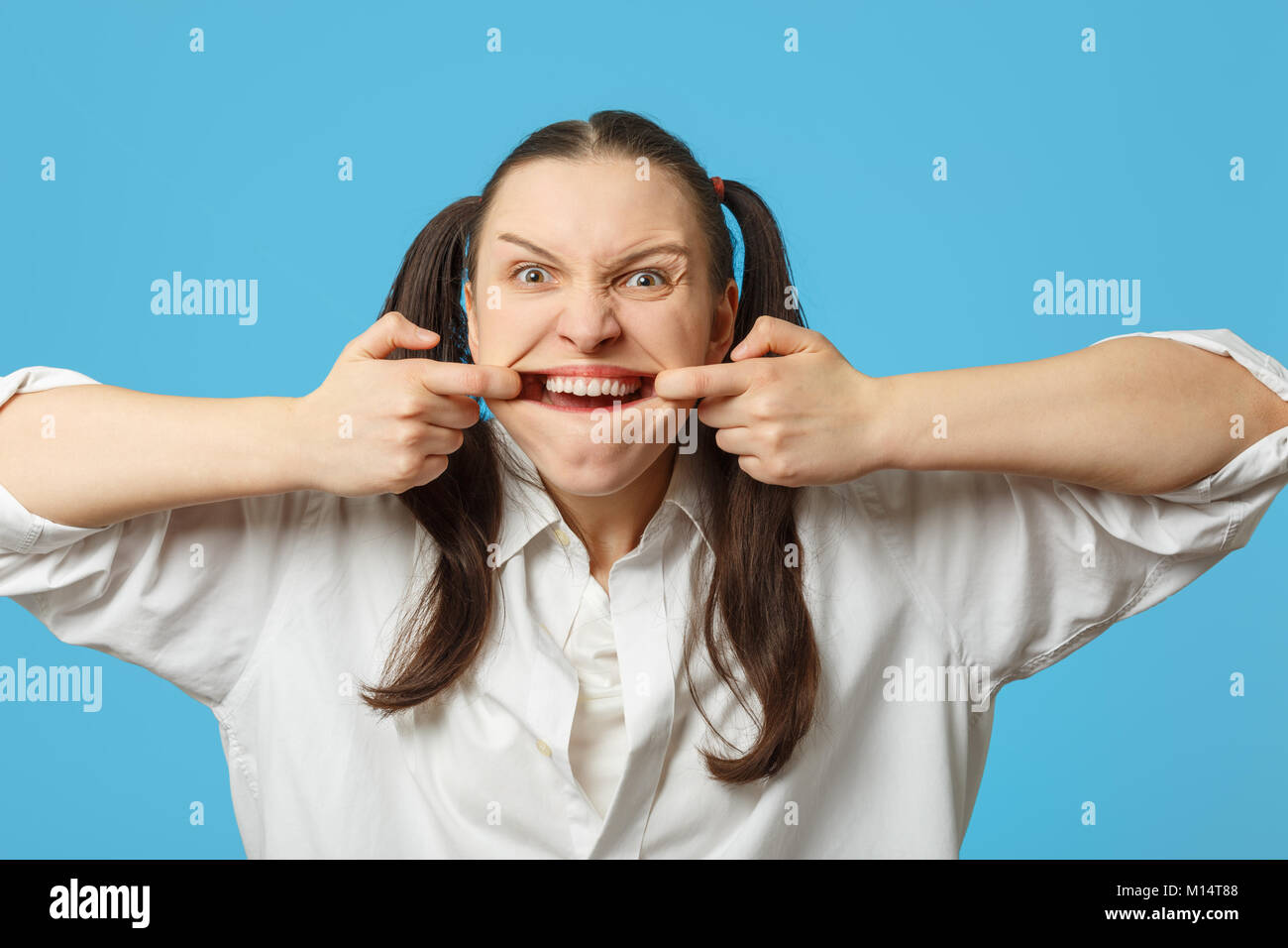 fun woman grimacing shows her teeth on blue background Stock Photo - Alamy
