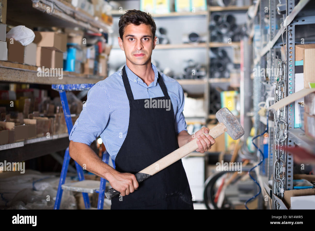 Portrait of builder male who is choosing sledgehammer in building shop ...