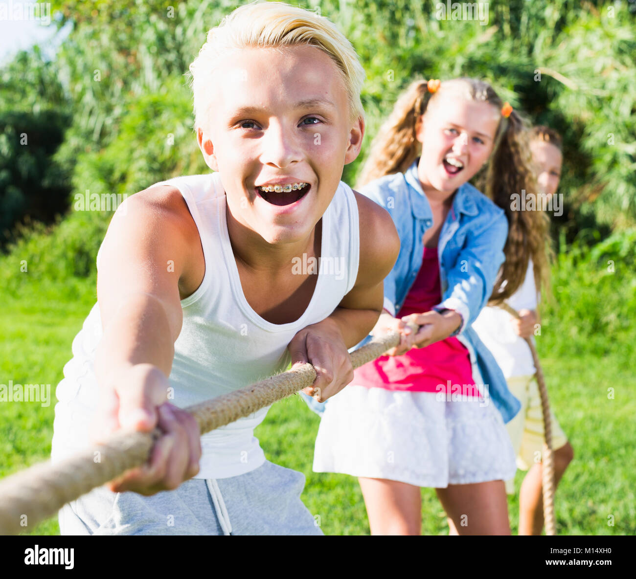 Group of laughing children having fun together outdoors pulling rope ...