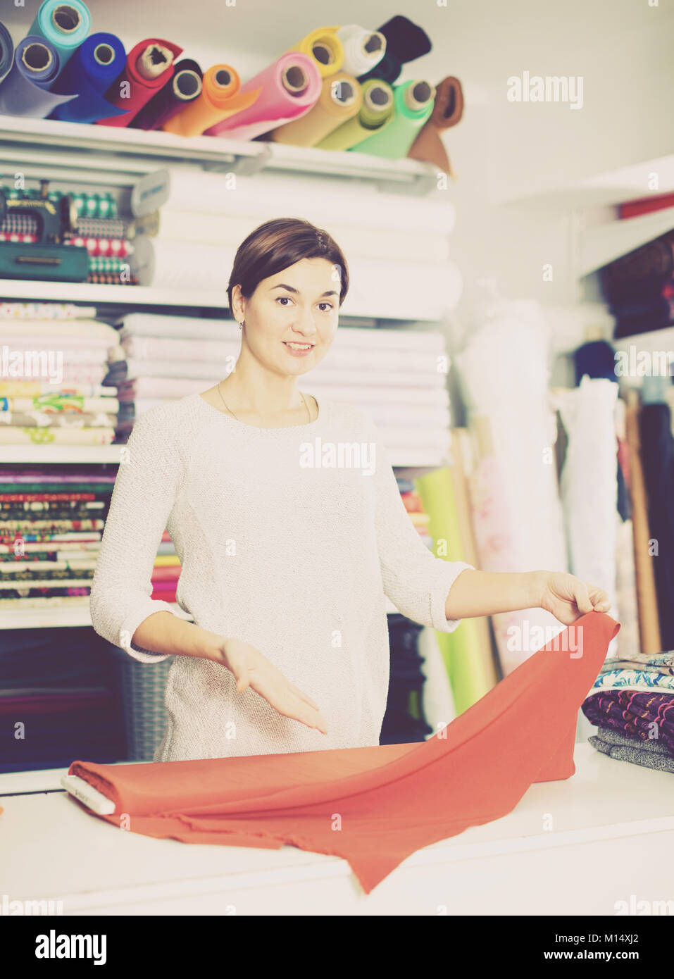 Young woman seller measuring square of cloth at drapery shop Stock ...